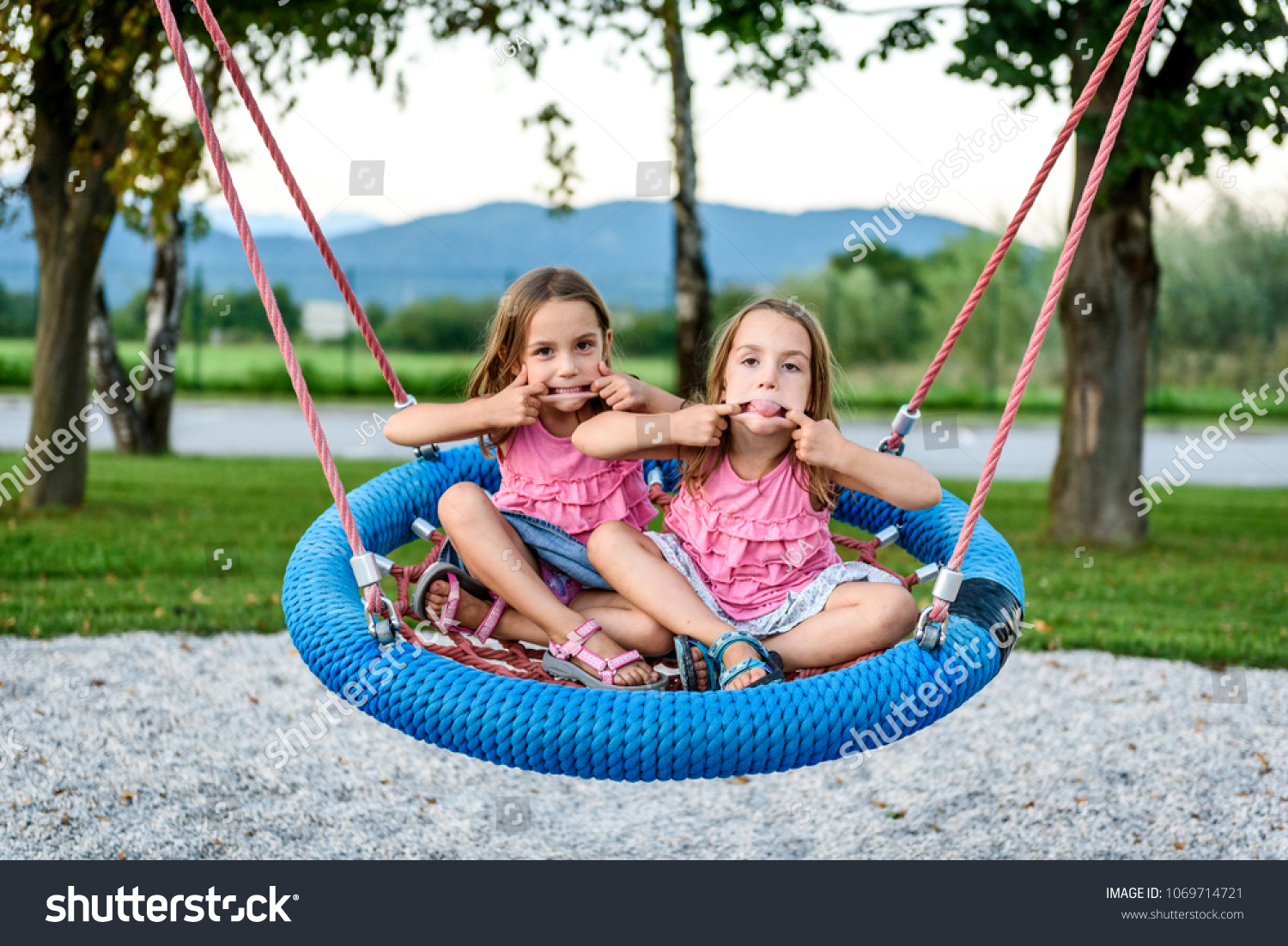 Identical twin girls on spider web nest swing on playground. Active Children playing with Giant ...