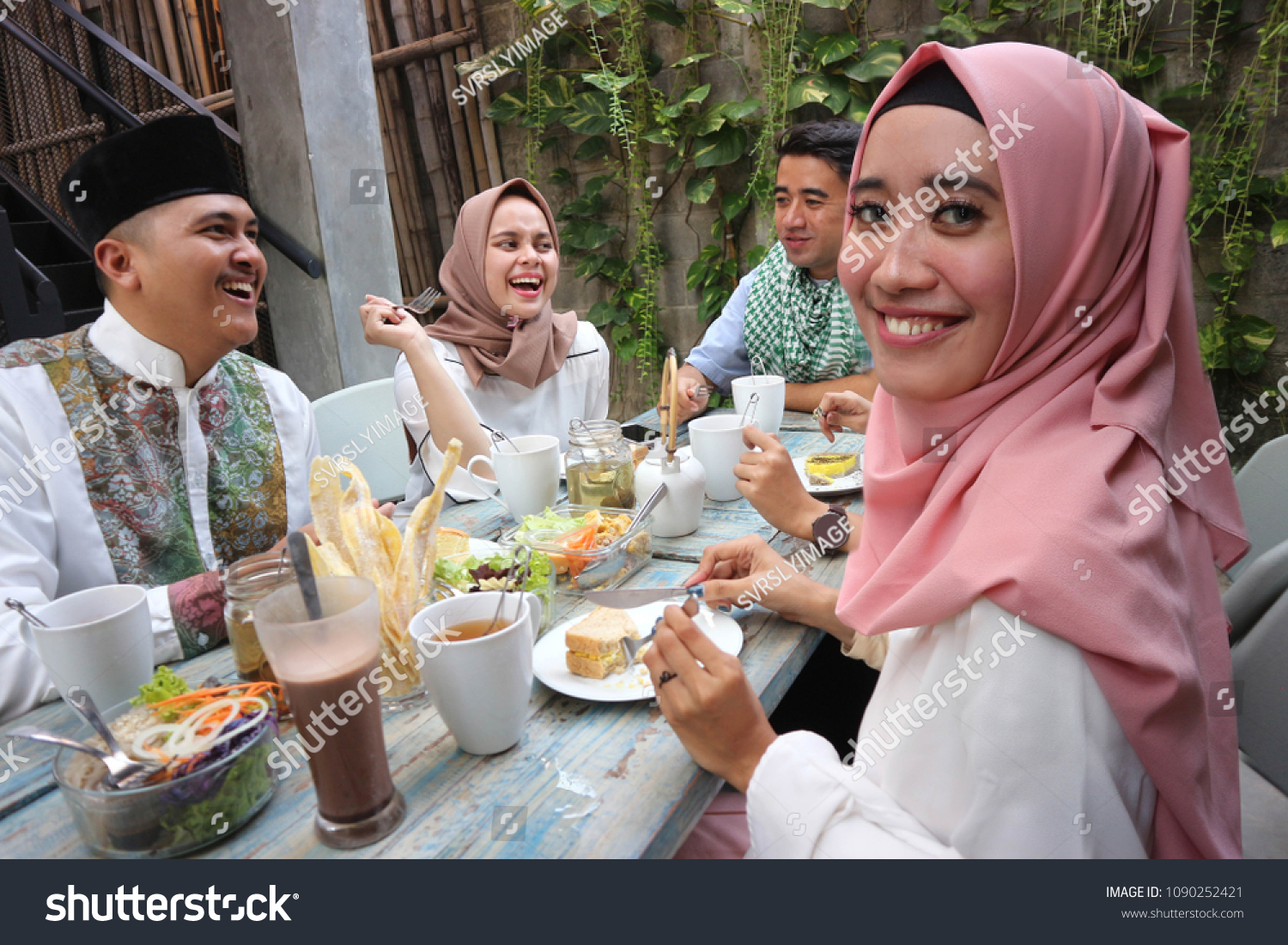 portrait of young muslim woman looking at camera while other pople eating during ramadan ...