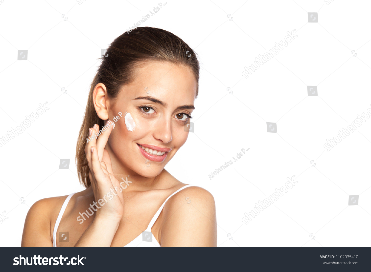 Beautiful woman applying moisturizing cream on her face on isolated background. Skin care and ...
