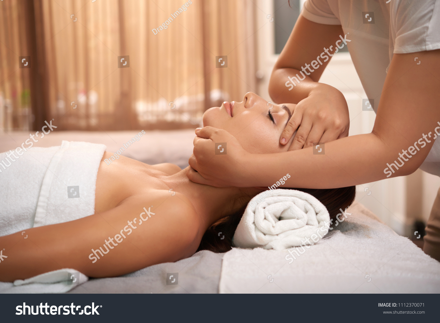 Young woman having calming massage on her face while relaxing in ...