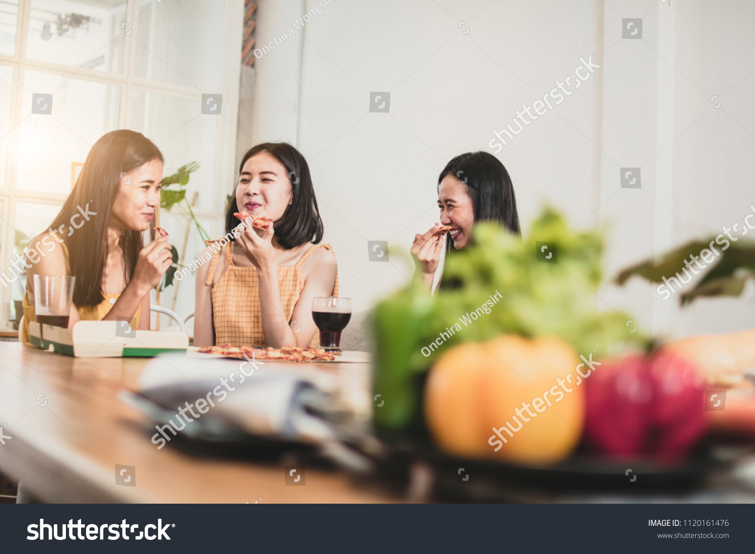group of Thai Asian funny women enjoying eating pizza and playing phone at home and don't care ...