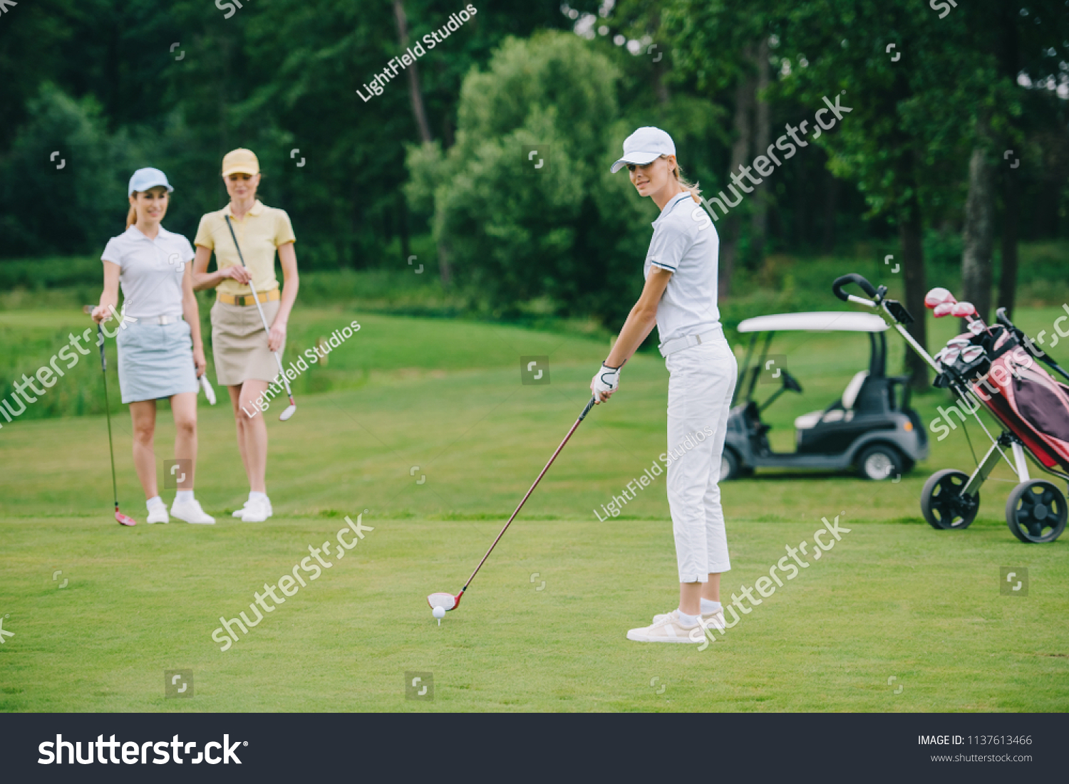 selective focus of woman in cap playing golf while friends standing near by at golf course_站酷海洛 ...