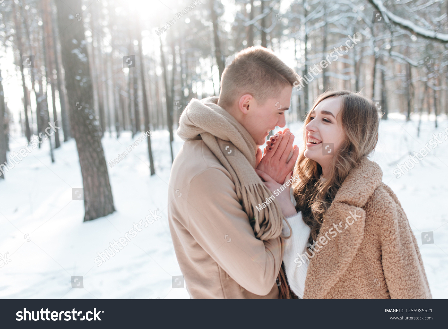 Young boy is kissing and hugging girls hands in a winter pine forest on holiday. Young people ...