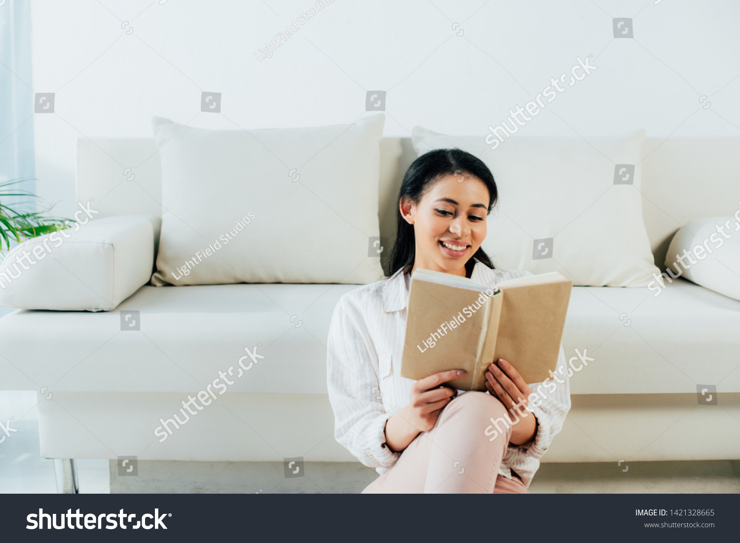 cheerful latin woman reading book while sitting on floor near couch_站酷海洛_正版图片_视频_字体_音乐素材交易平台_站酷旗下品牌