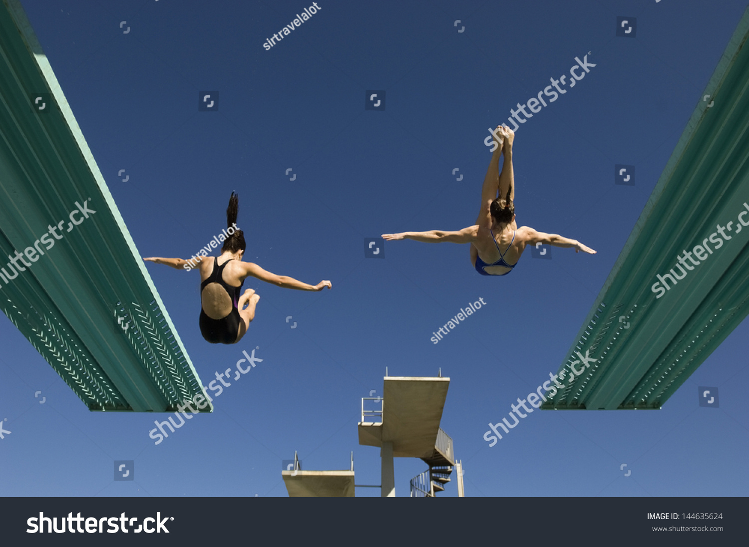 Rear view of two women diving from diving boards against clear blue sky ...
