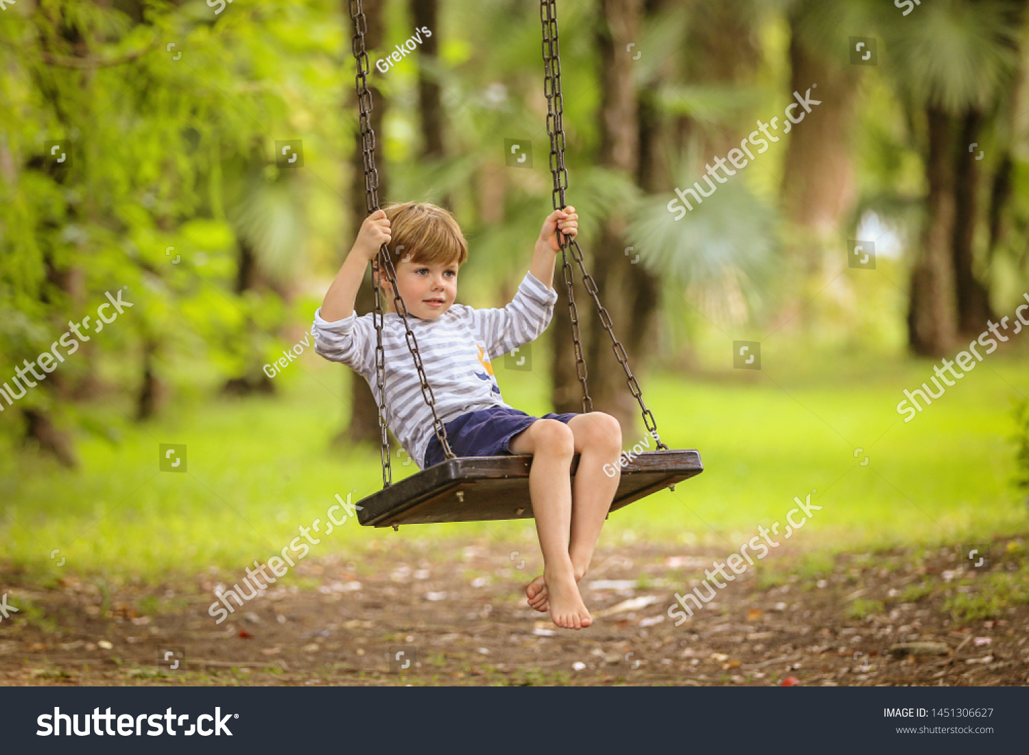 A handsome boy rides a long swing surrounded by palm trees and trees. Picturesque paradise of ...