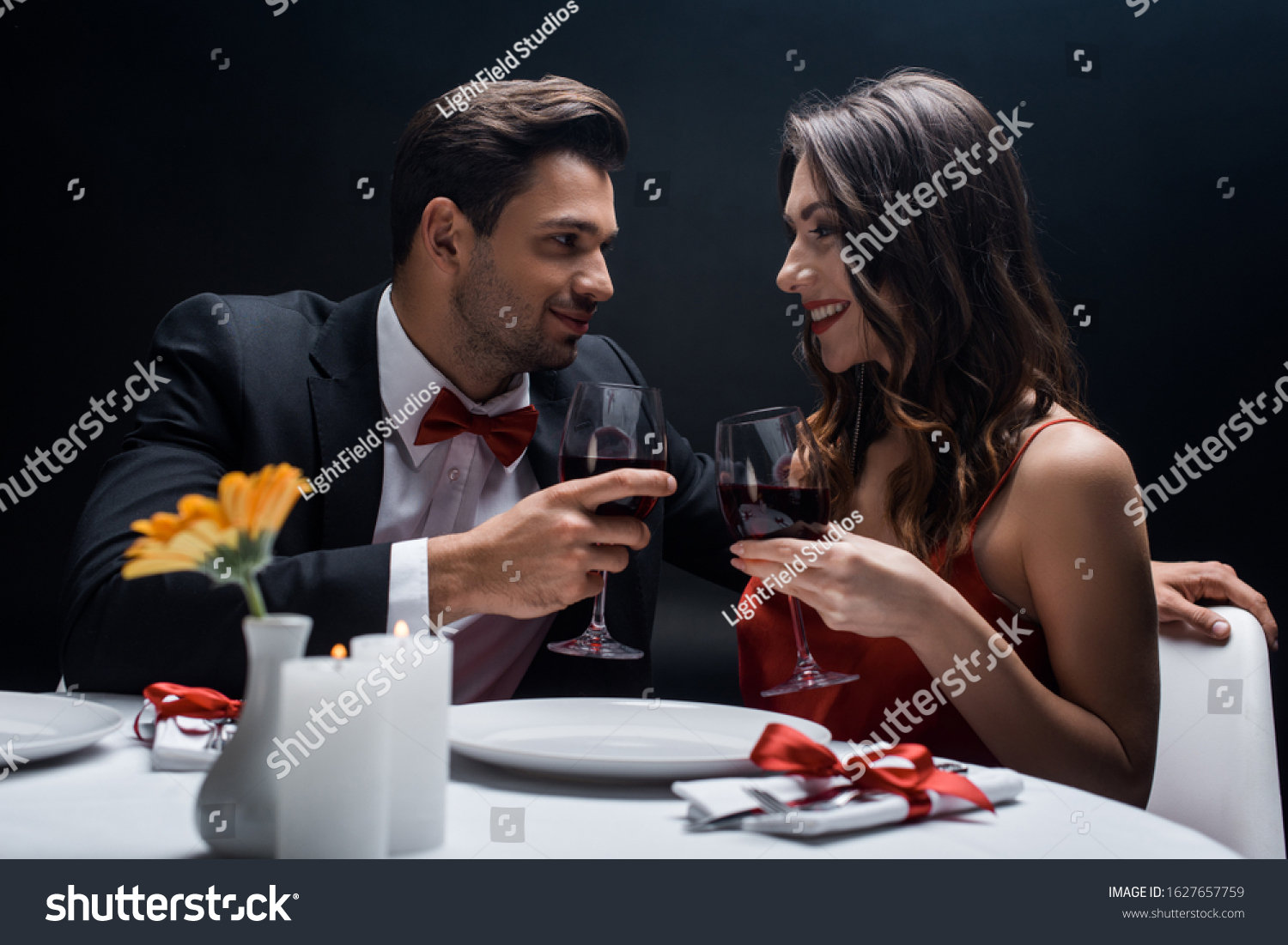 Side view of smiling couple with wine glasses looking at each other at ...