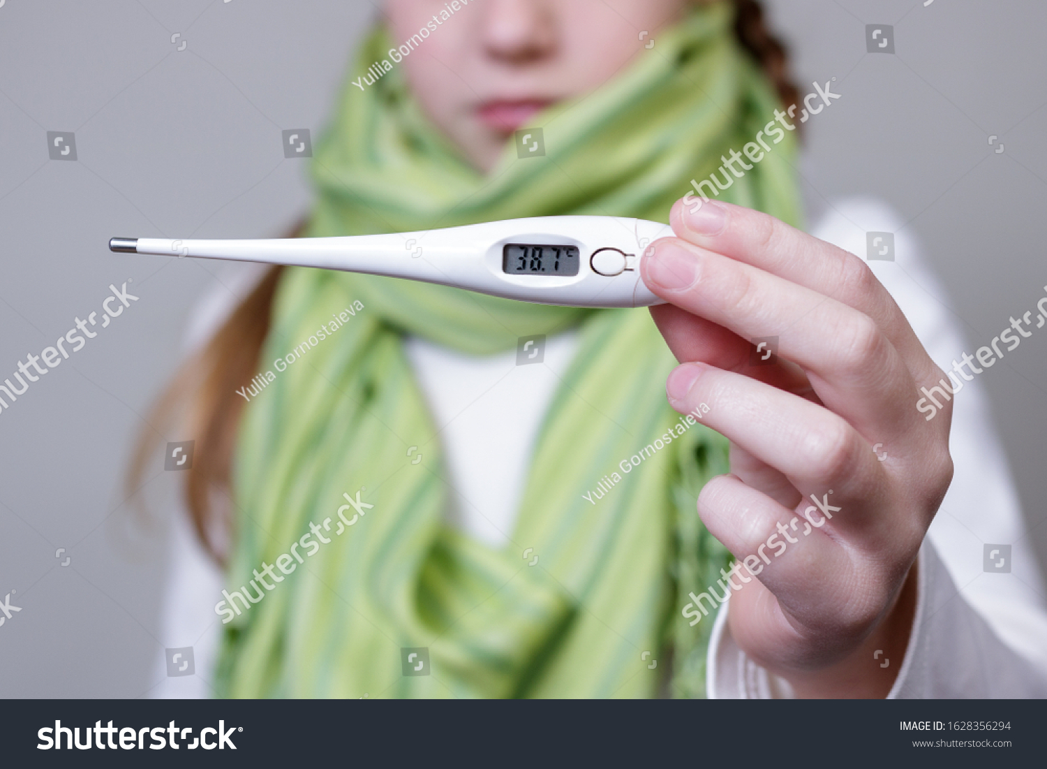 Sick sad red-haired girl of 9 years old in light clothes and a green scarf shows a digital ...