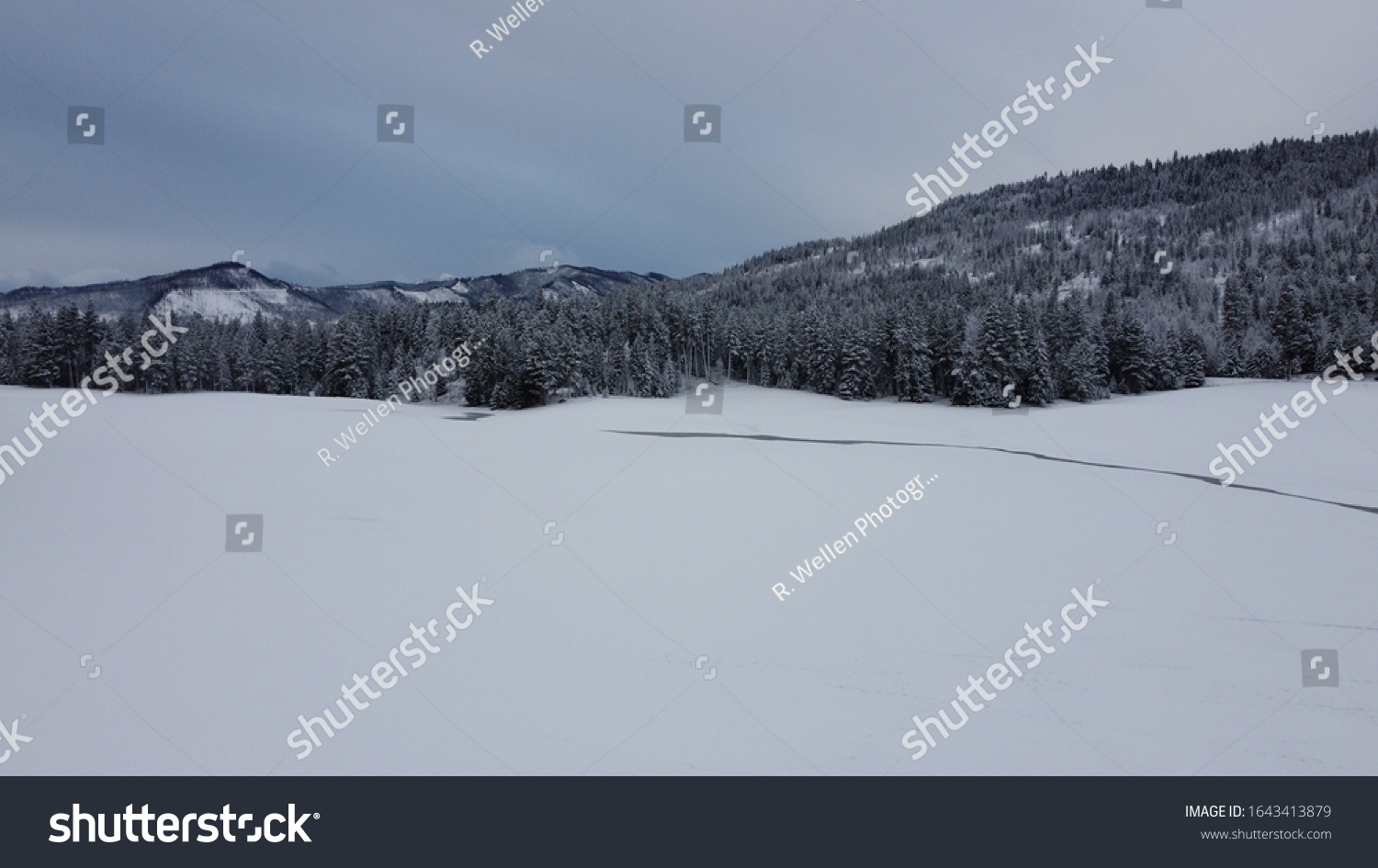 Large snow covered field with stream cutting through in front of snow ...