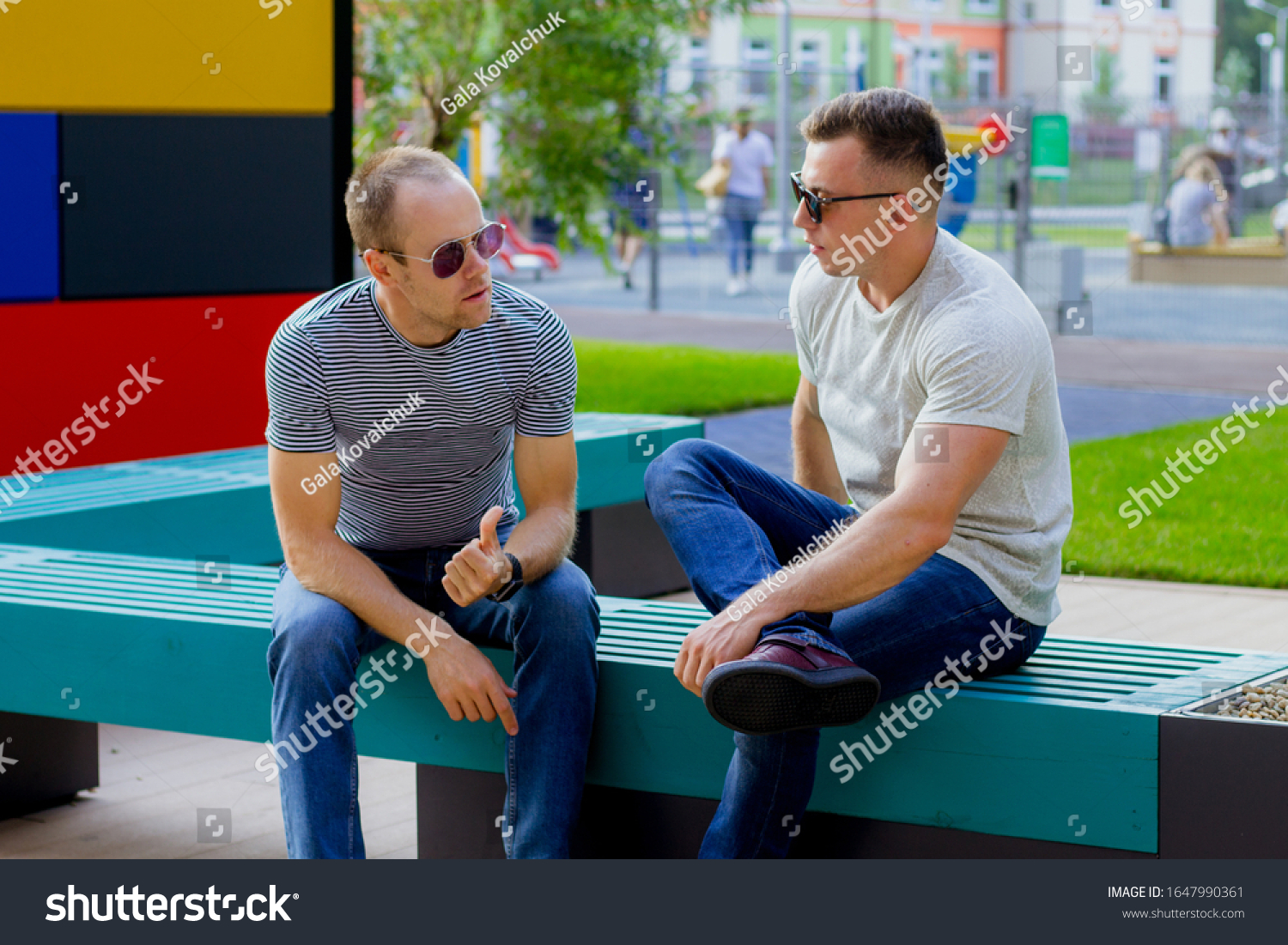 Two young men talking to each other in a park .Friends meeting outside ...