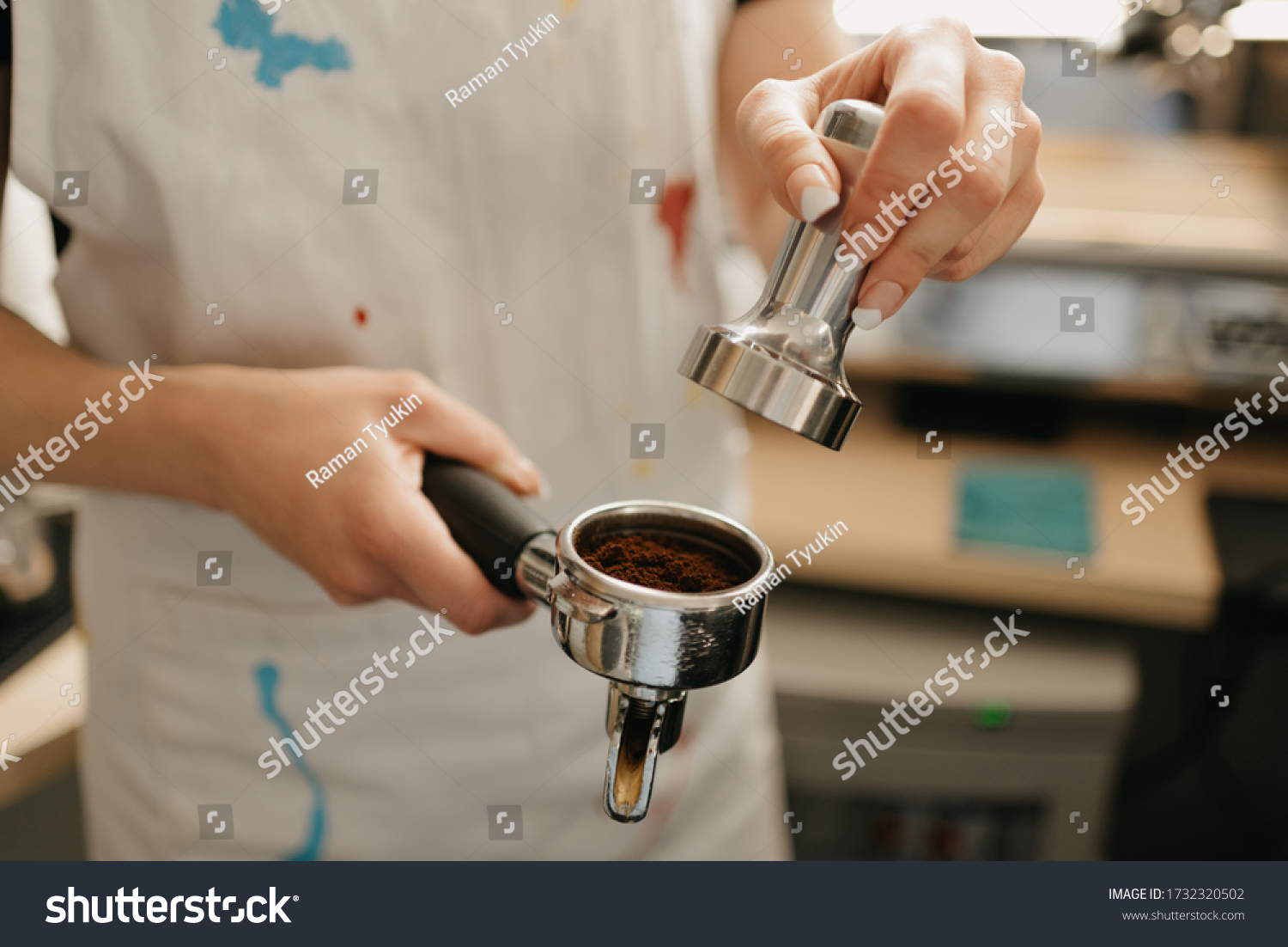 A female barista holds a metal tamper and a portafilter with coffee in ...