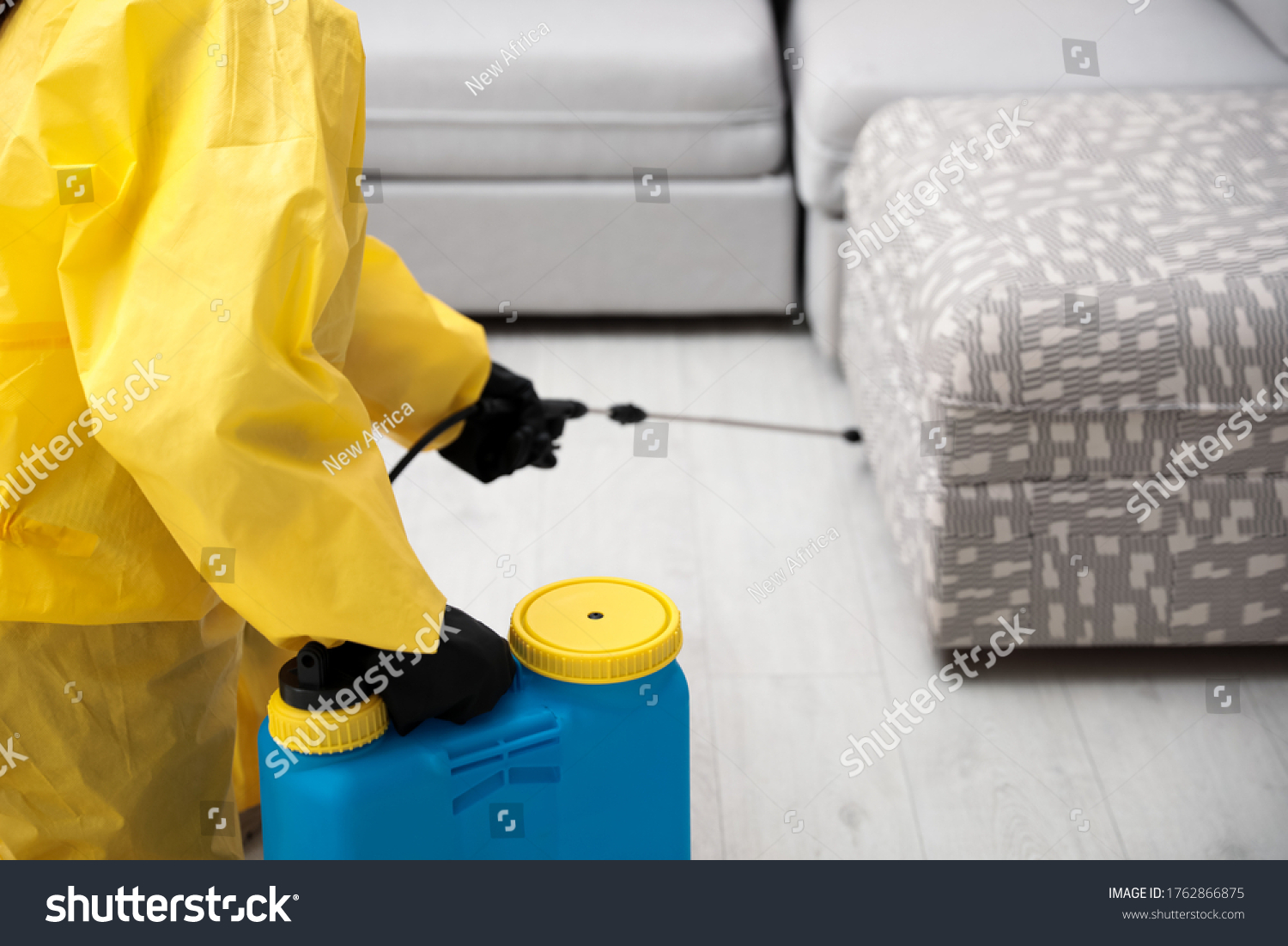 Pest control worker spraying pesticide under furniture indoors closeup ...