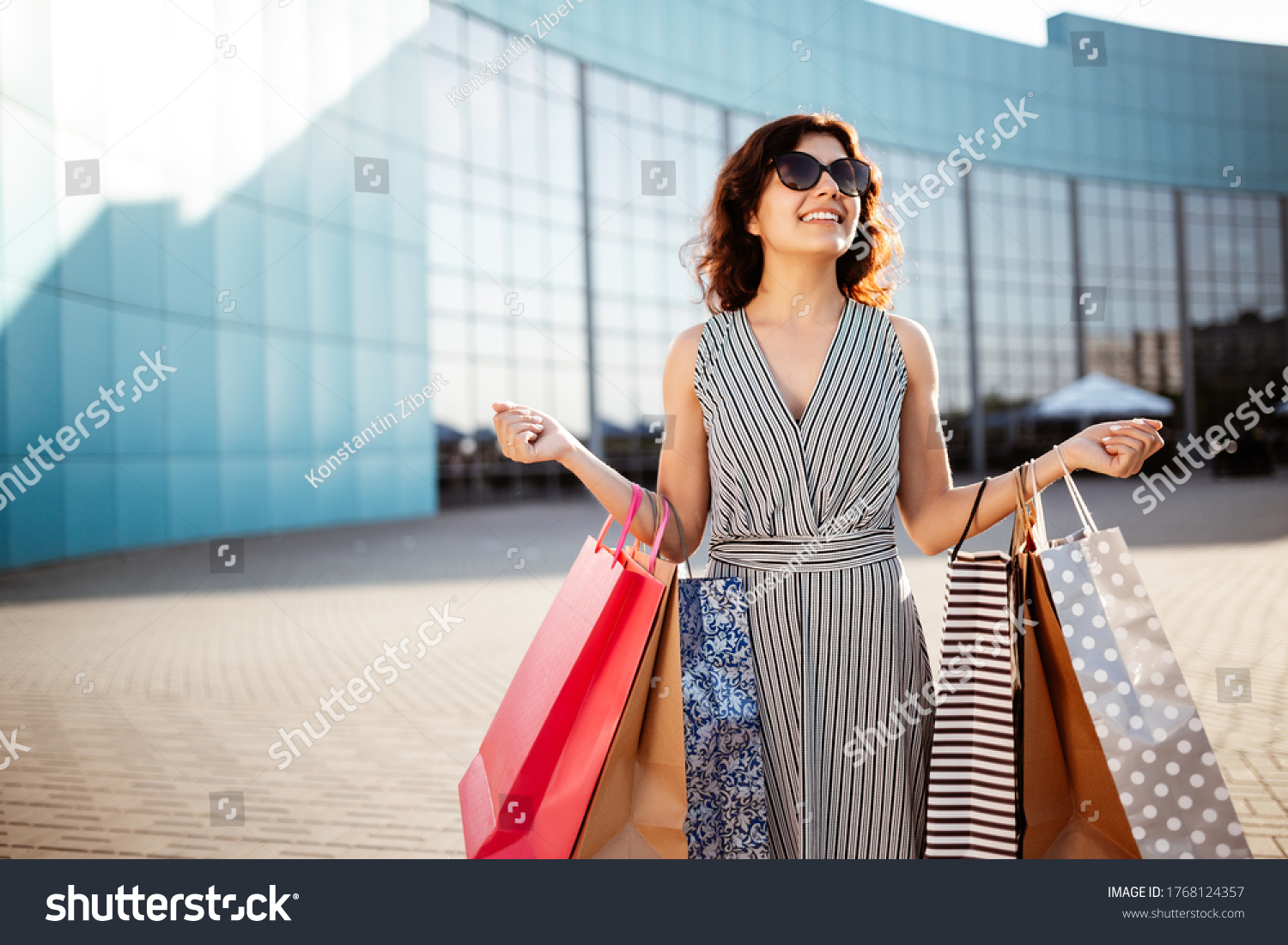 Young beautiful happy woman walks out of shopping mall with purchases ...