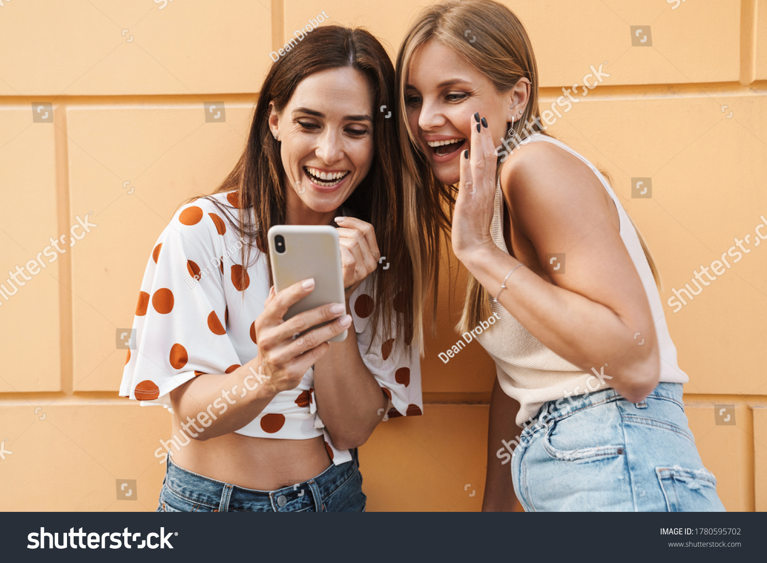 Image of cheerful adult two women using mobile phone and laughing while posing on city street_站酷 ...