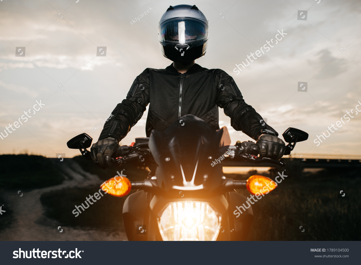 Close-up photo of biker sitting on motorcycle in sunset on the country ...
