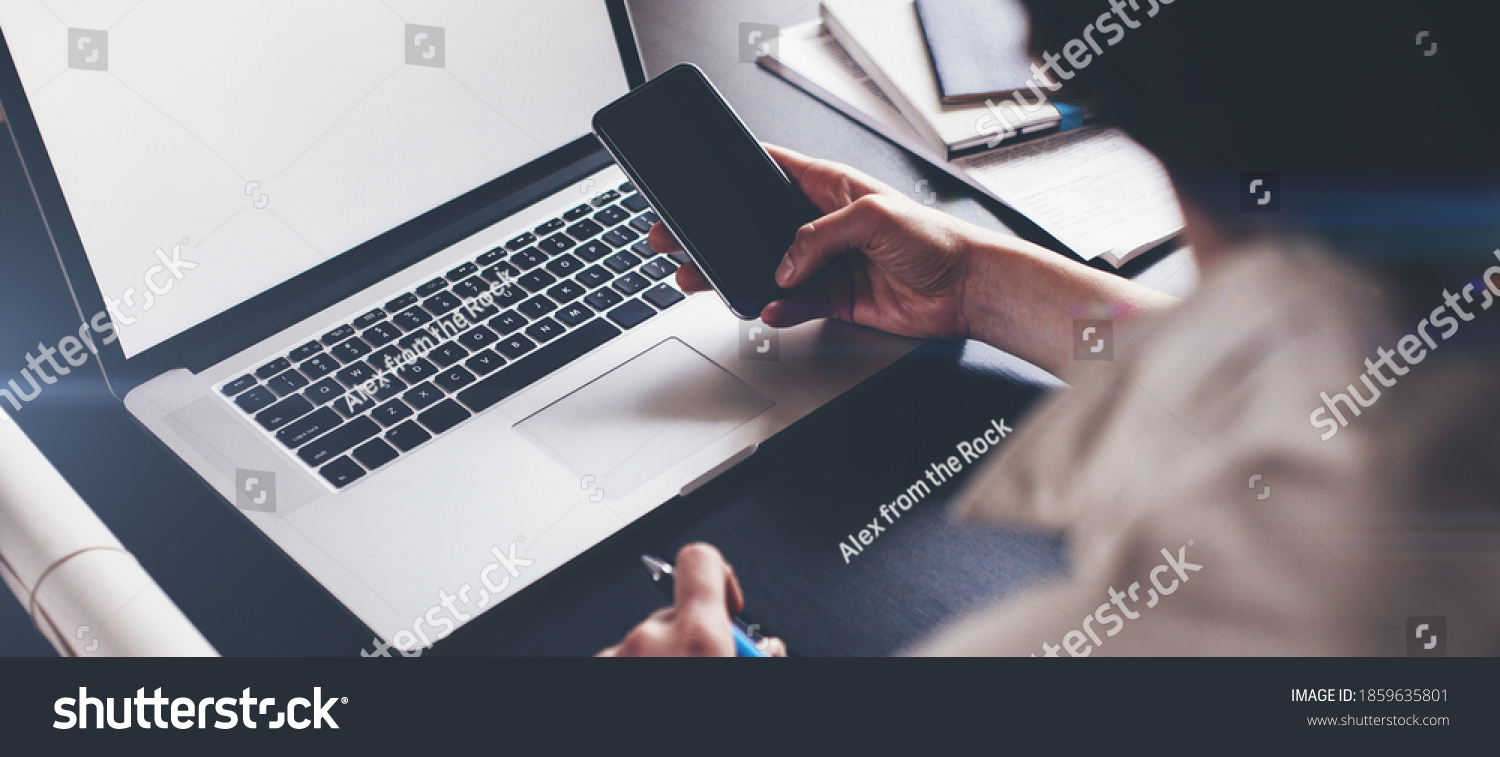 Woman with laptop distant working alone. Holding mobile phone and pen ...