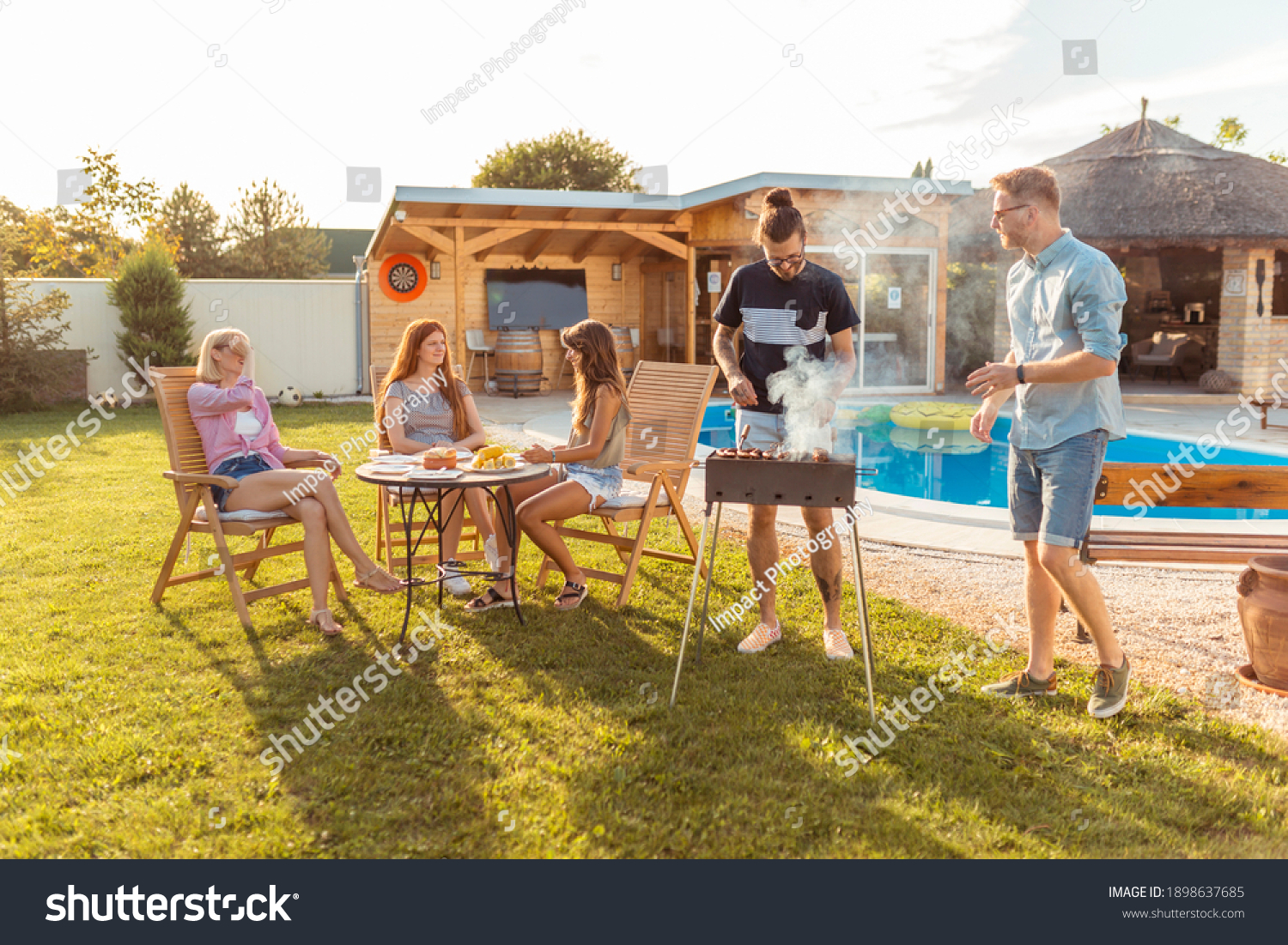 Group of young friends having a backyard barbecue party grilling meat and having fun while ...