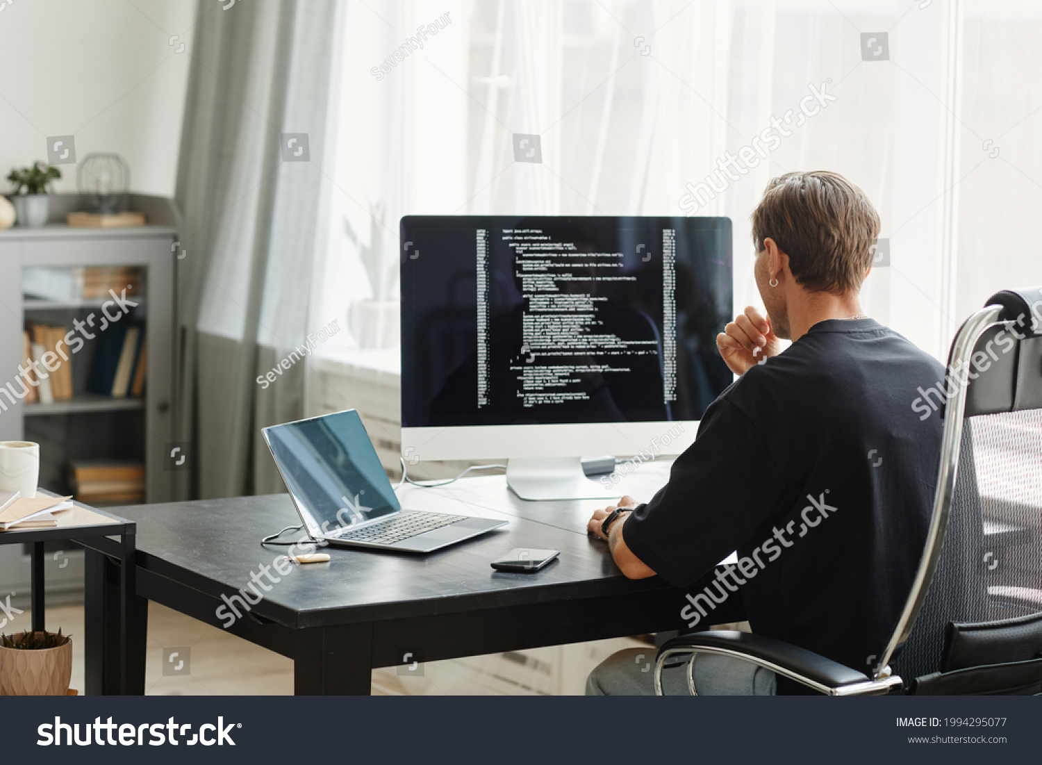 Rear view of computer programmer sitting at the table in front of ...