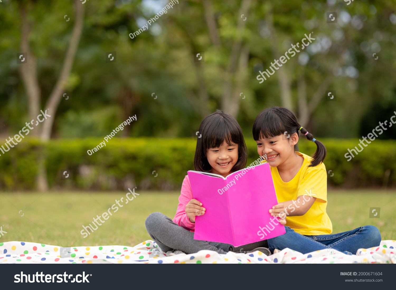 two beautiful little girls reading books in the garden sitting on grass. The concept of ...