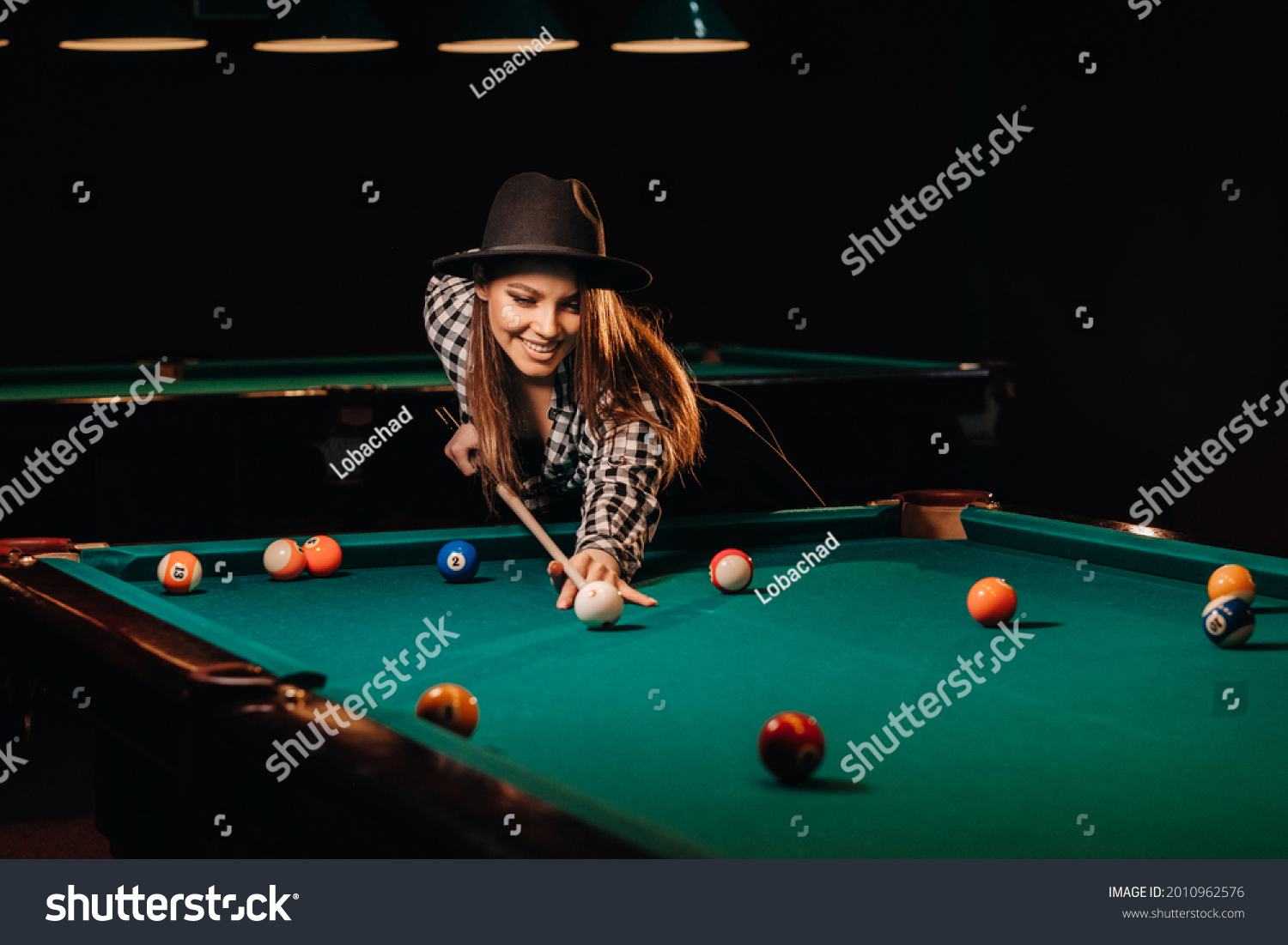A girl in a hat in a billiard club with a cue in her hands hits a ball.Playing billiards._站酷海洛 ...
