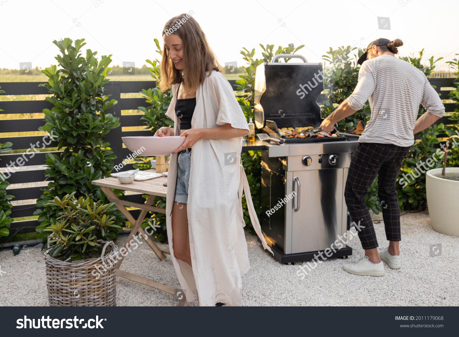 Man cooking on the modern gas grill at beautiful backyard on a sunset. Cooking food on the open ...