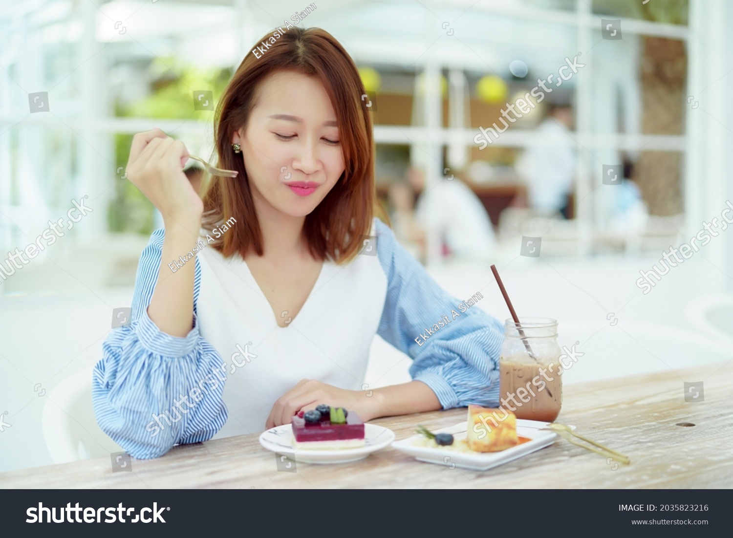 A beautiful Asian portrait is taking a spoonful of cakes on the table and eating them with happy ...