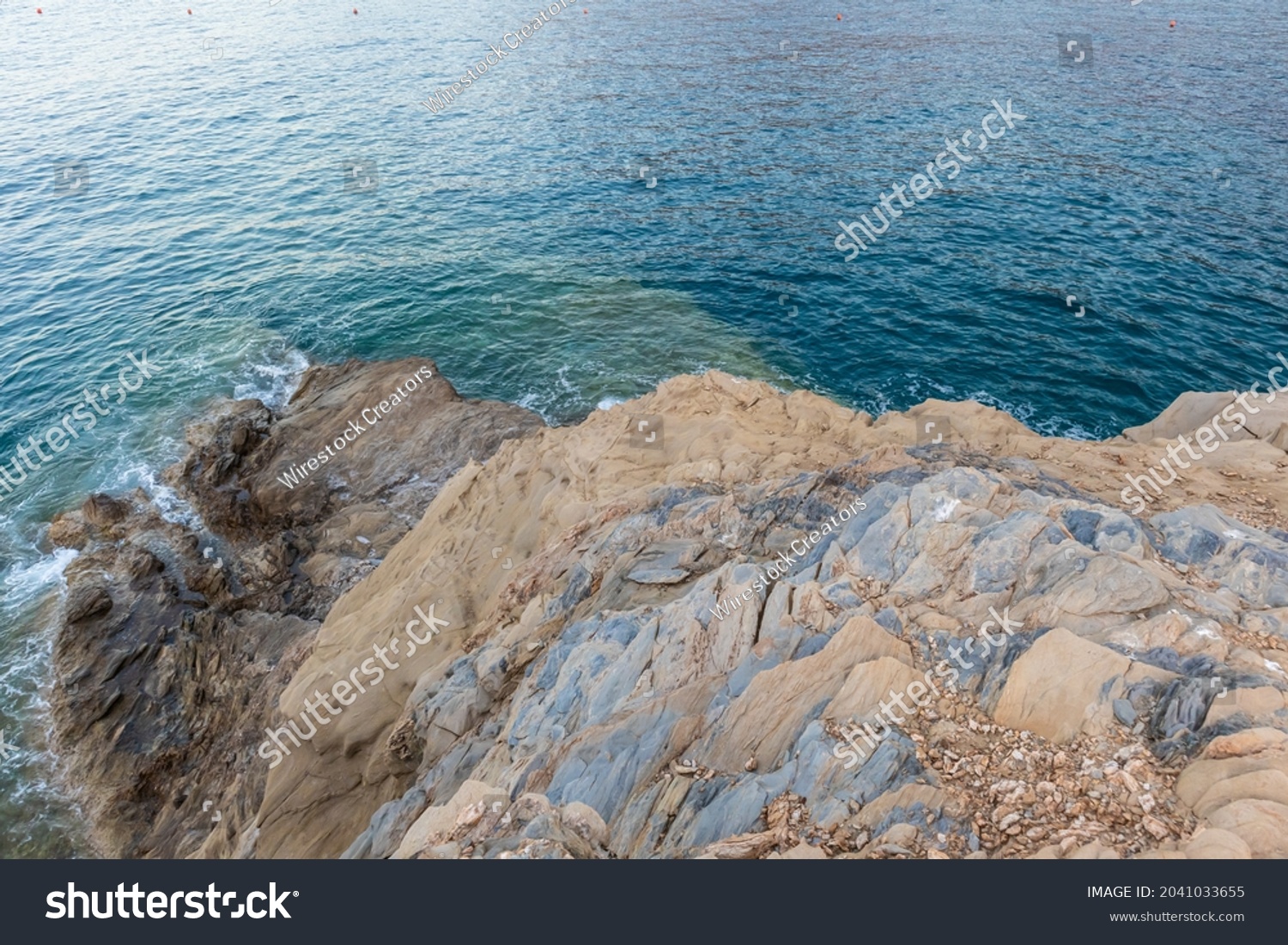 A beautiful view from the top of a rocky cliff on blue water and rocky ...