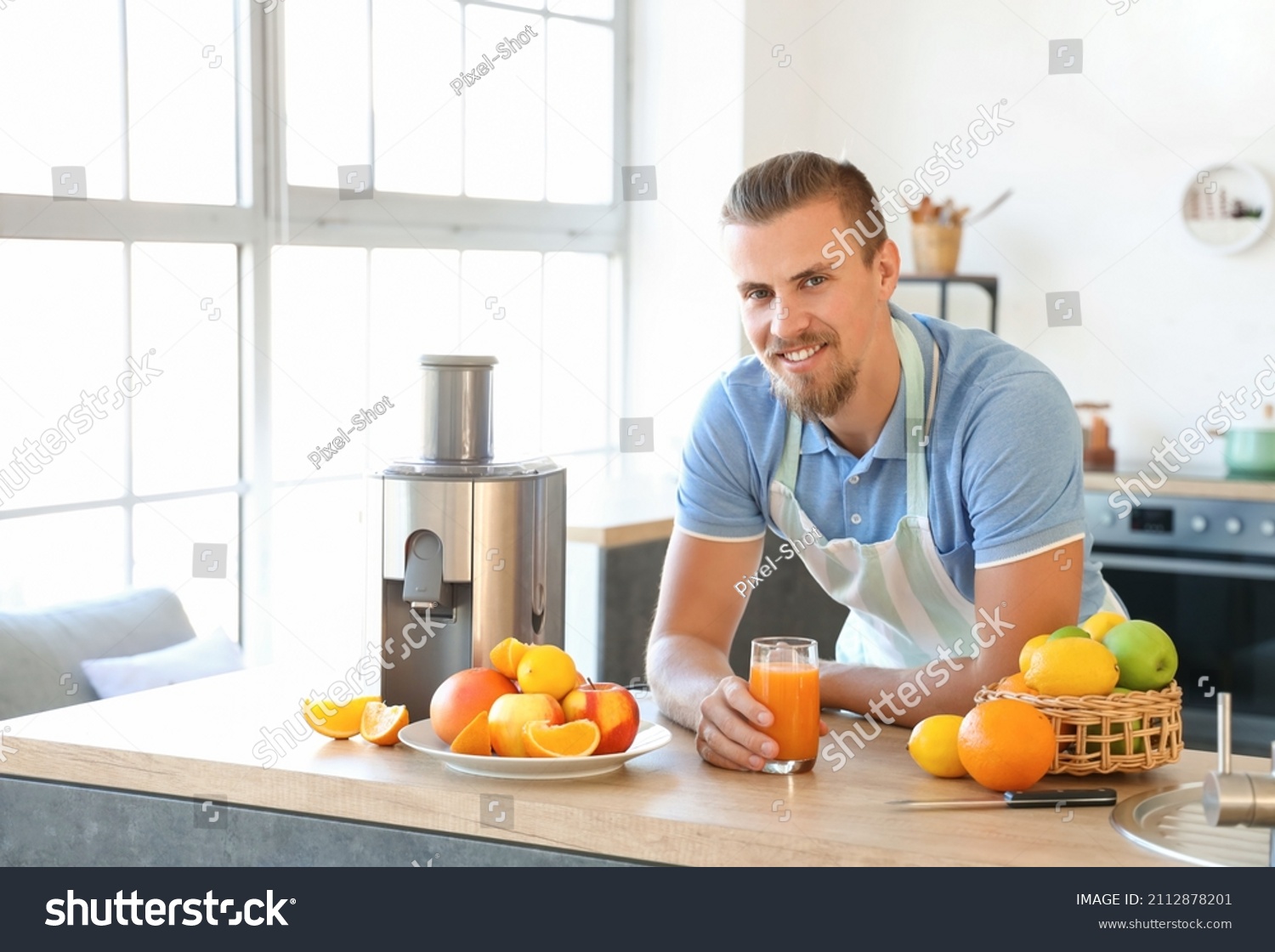 Young man with glass of fresh fruit juice near modern juicer in kitchen ...