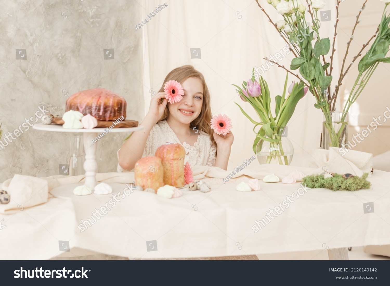 A girl with long hair in a light dress is sitting at the Easter table ...