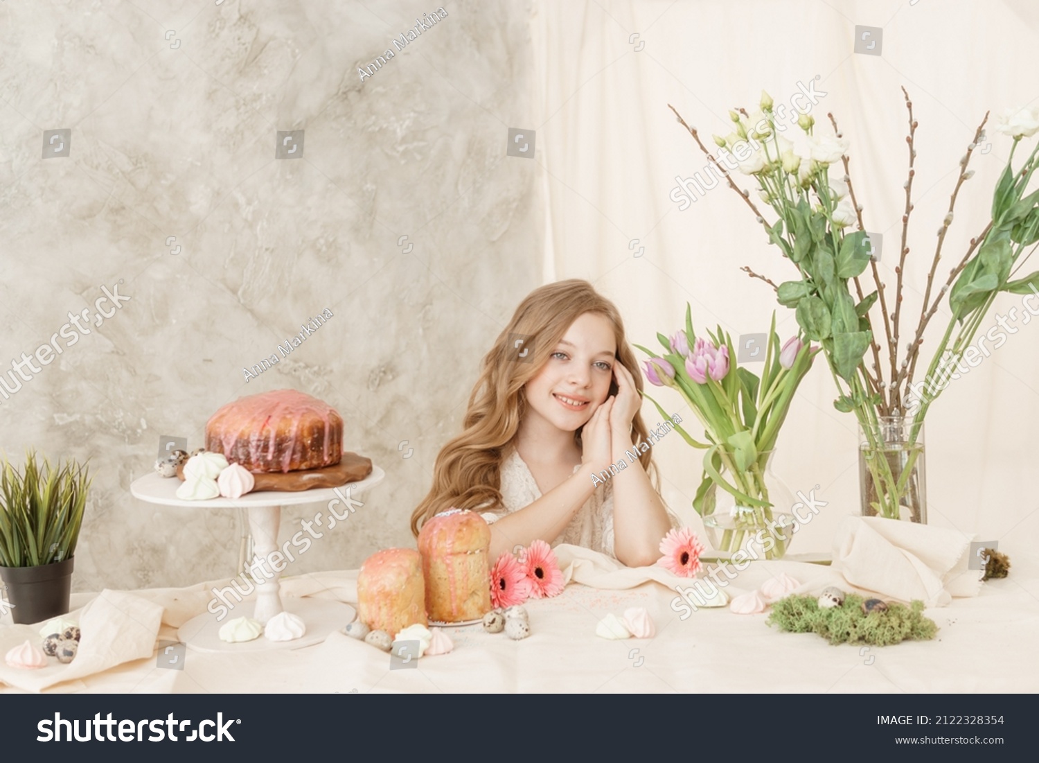 A girl with long hair in a light dress is sitting at the Easter table ...
