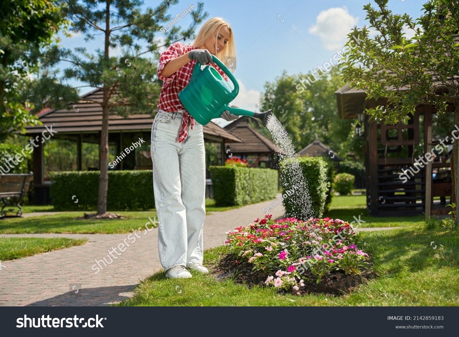 Happy caucasian woman in casual wear and gloves using watering can for ...