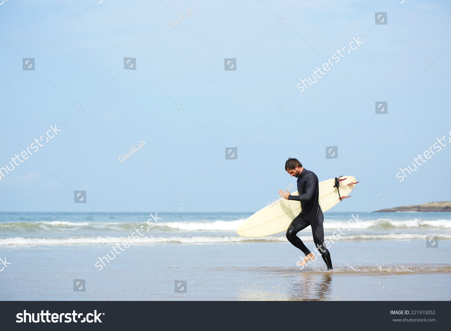Young surfer man carrying his surfing board running along the ocean to ...