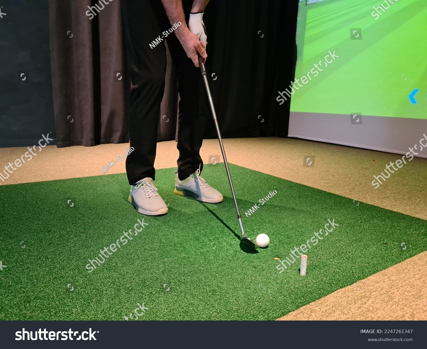 Golf player playing golf indoors on golf simulator closeup. Driving range with screen for golf ...