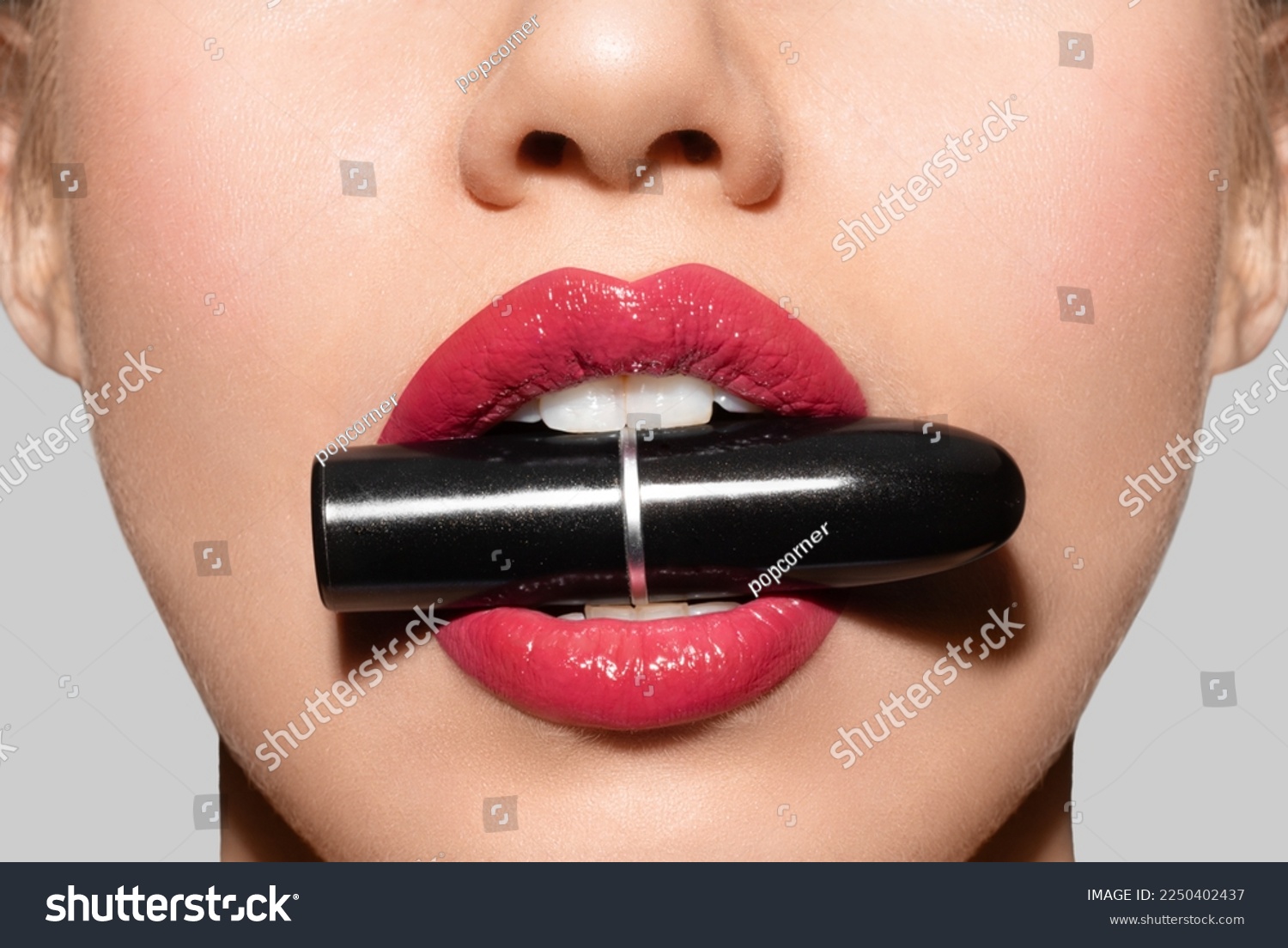 Close-up of the model's red lips holding the lipstick. Beautiful cosmetic macro portrait of a ...