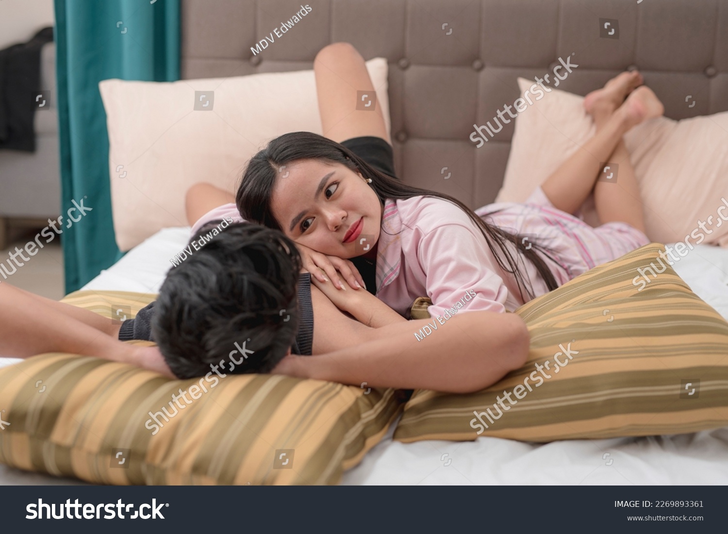 An affectionate couple looking fondly at each other while resting on the bed at their hotel room ...