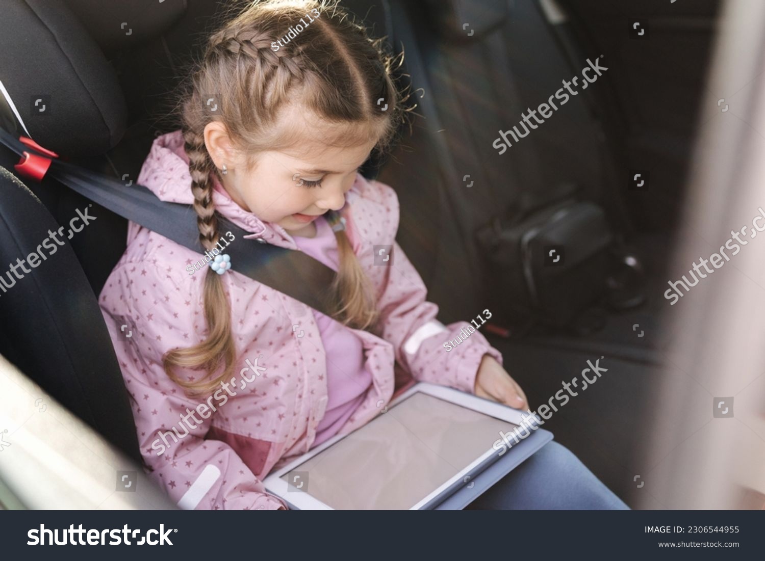 Beautiful little girl in car seat using digital tablet during trip ...