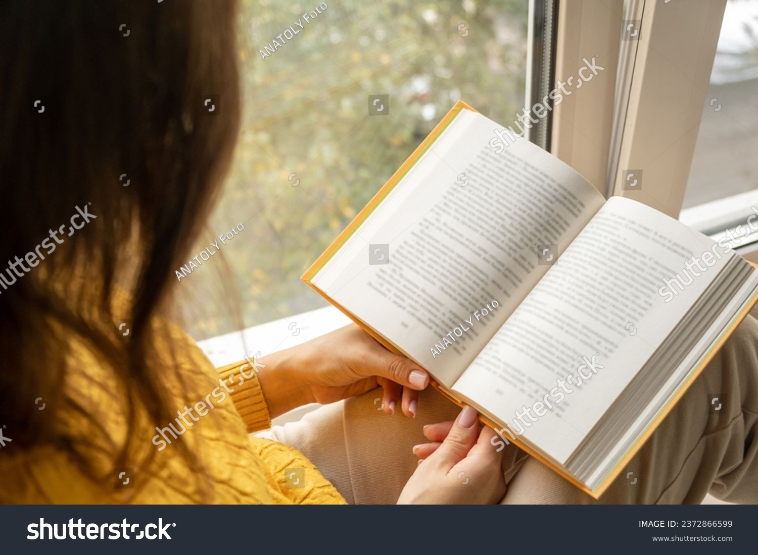 Young beautiful woman sitting by the window yellow knitted sweater read book daily planner ...