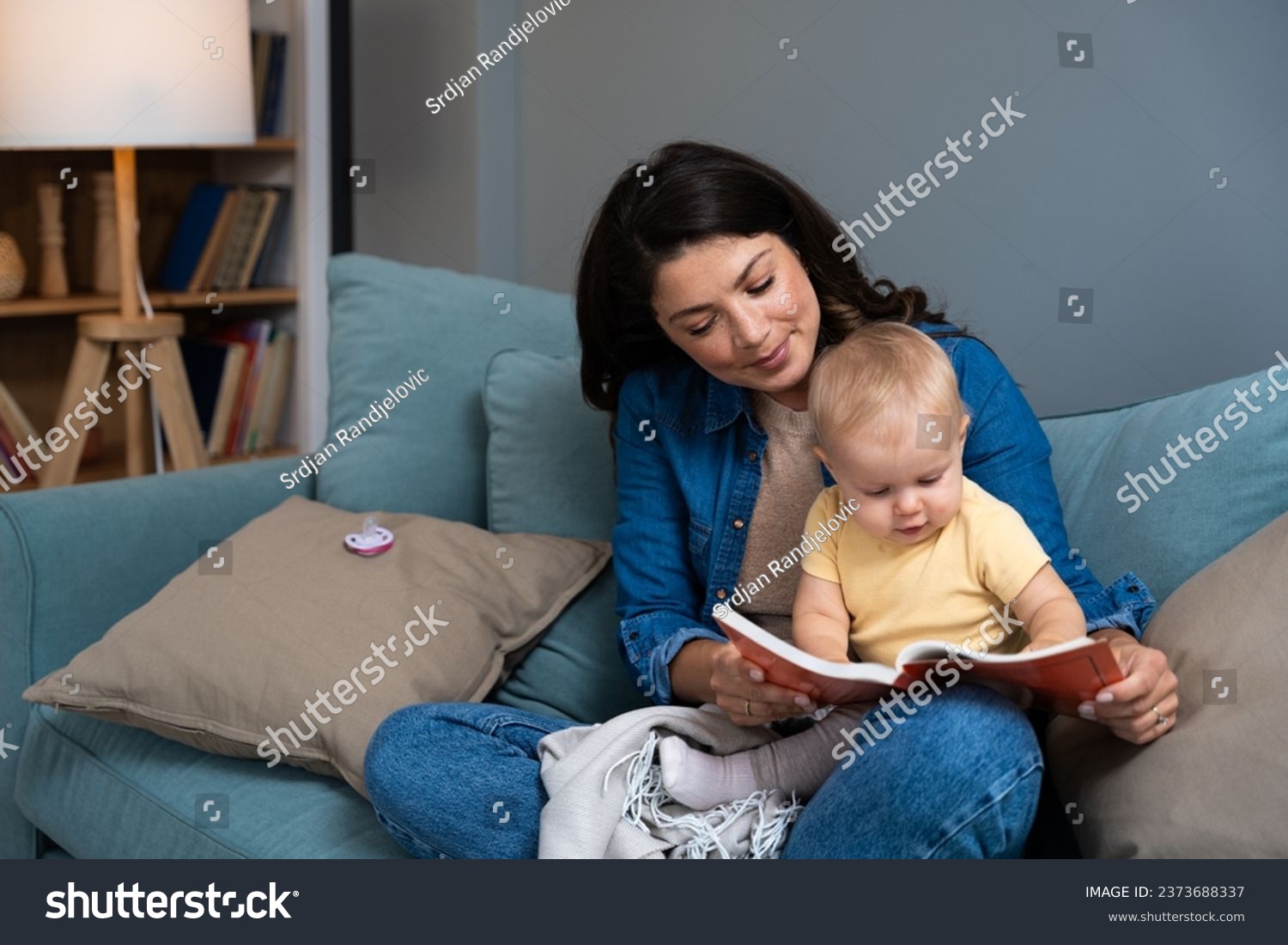 Mom reading a book with baby boy or girl at home. Early age children education development ...