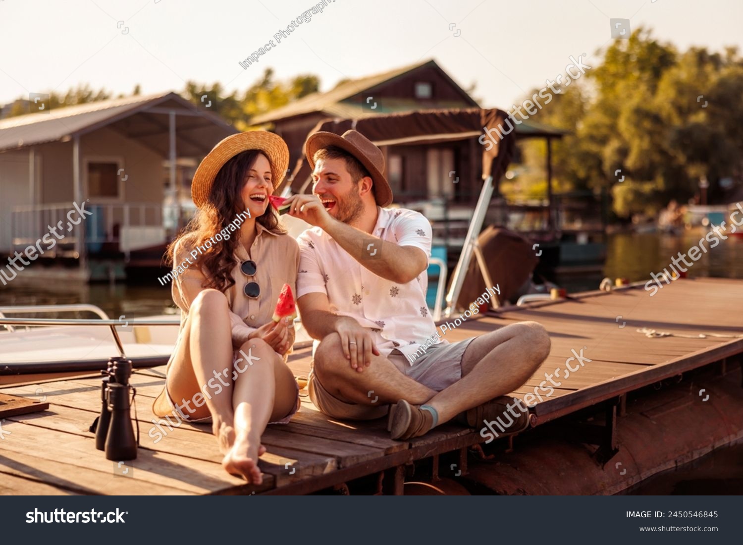 Beautiful young couple in love relaxing while on summer vacation sitting on river docks in city ...