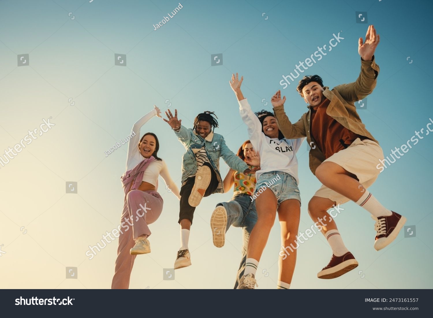 A group of cheerful young friends jumping together in joy celebrating ...