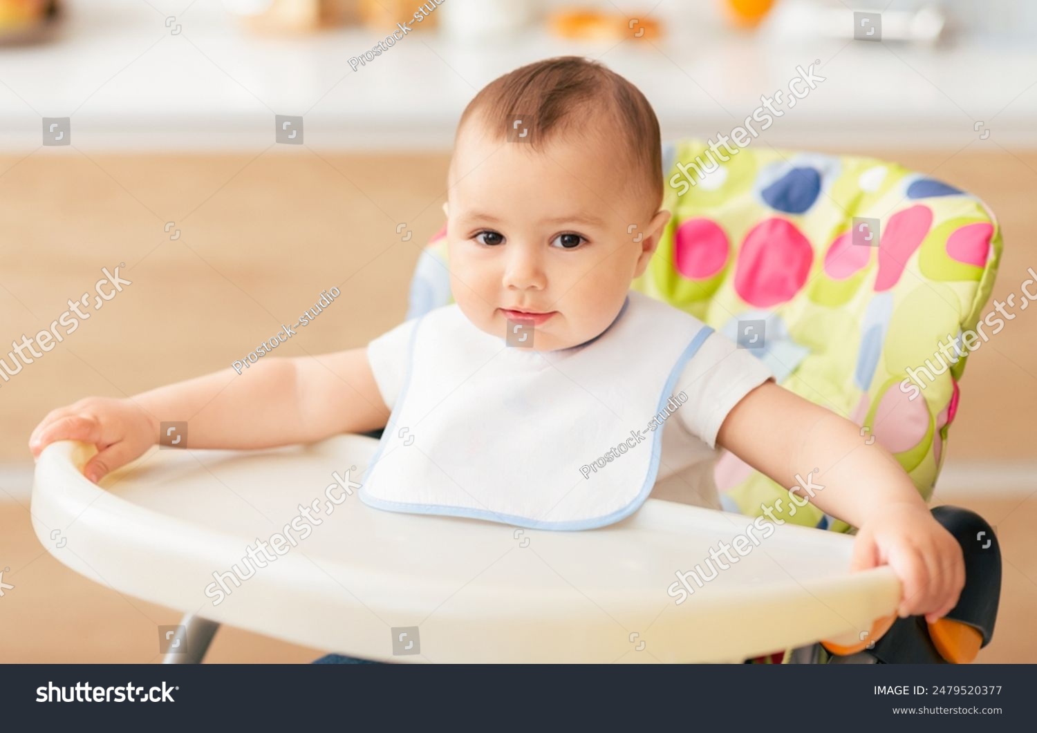 A cute baby wearing a white bib sits comfortably in a high chair in a ...