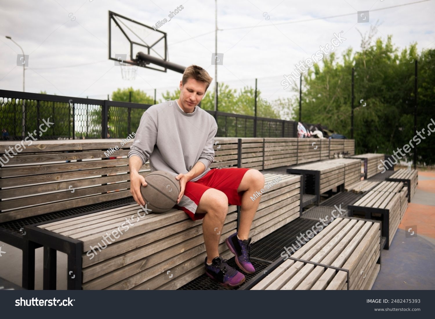young basketball player sits on a wooden bench at an outdoor court ...