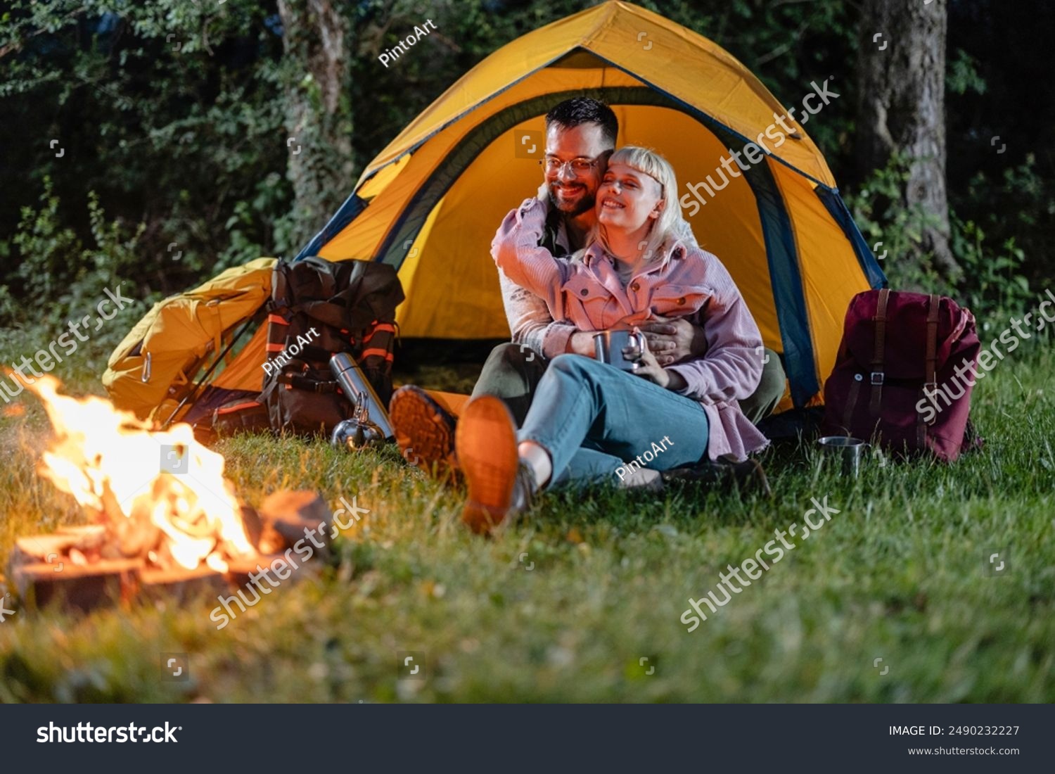 Smiling couple cuddling near a campfire in front of their tent enjoying ...