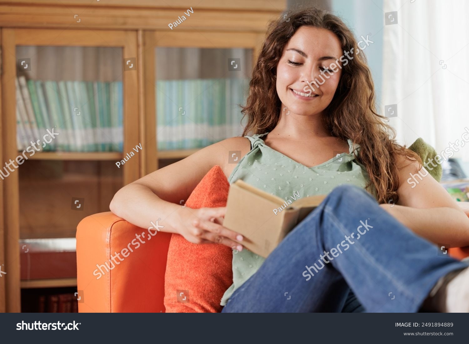 Young woman on the couch reading her favorite book. Student lying on the sofa in the library ...