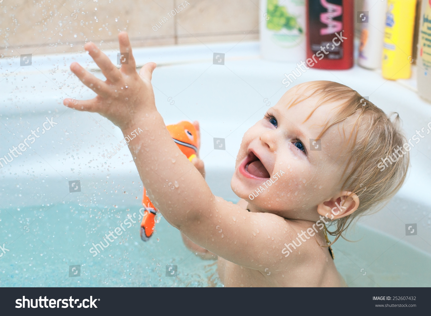 Funny little baby girl in the bath playing with water drops and ...