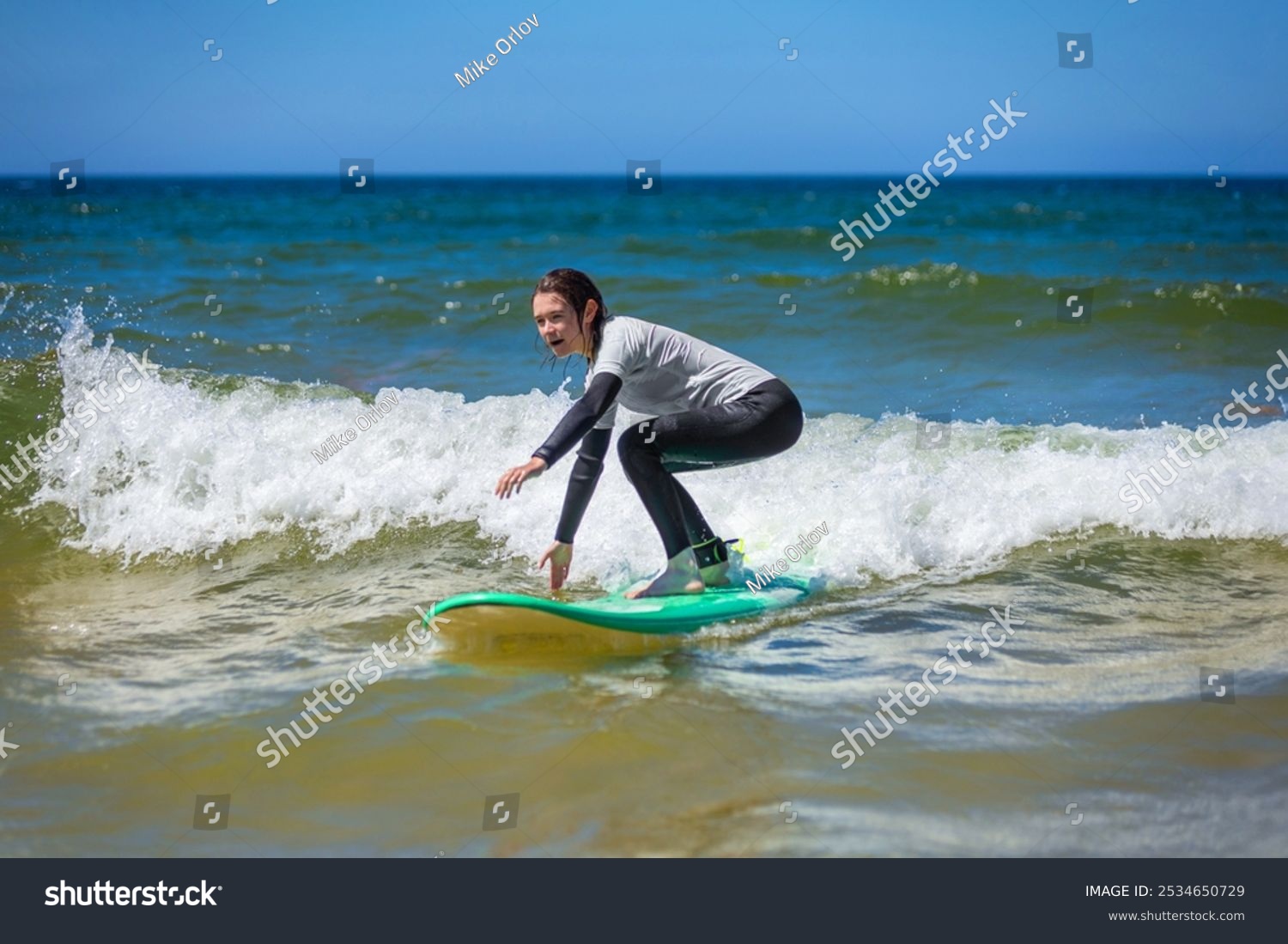 Surfer. Teenage girl learning to surf on foam in the ocean. First surfing lesson. Amateur surfer ...