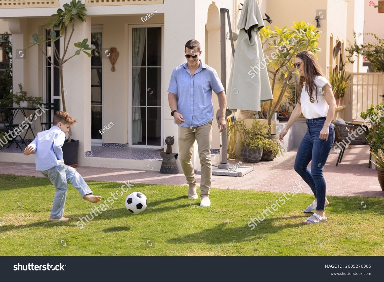 Mother father and their son play soccer together in backyard of their home kick ball moving ...