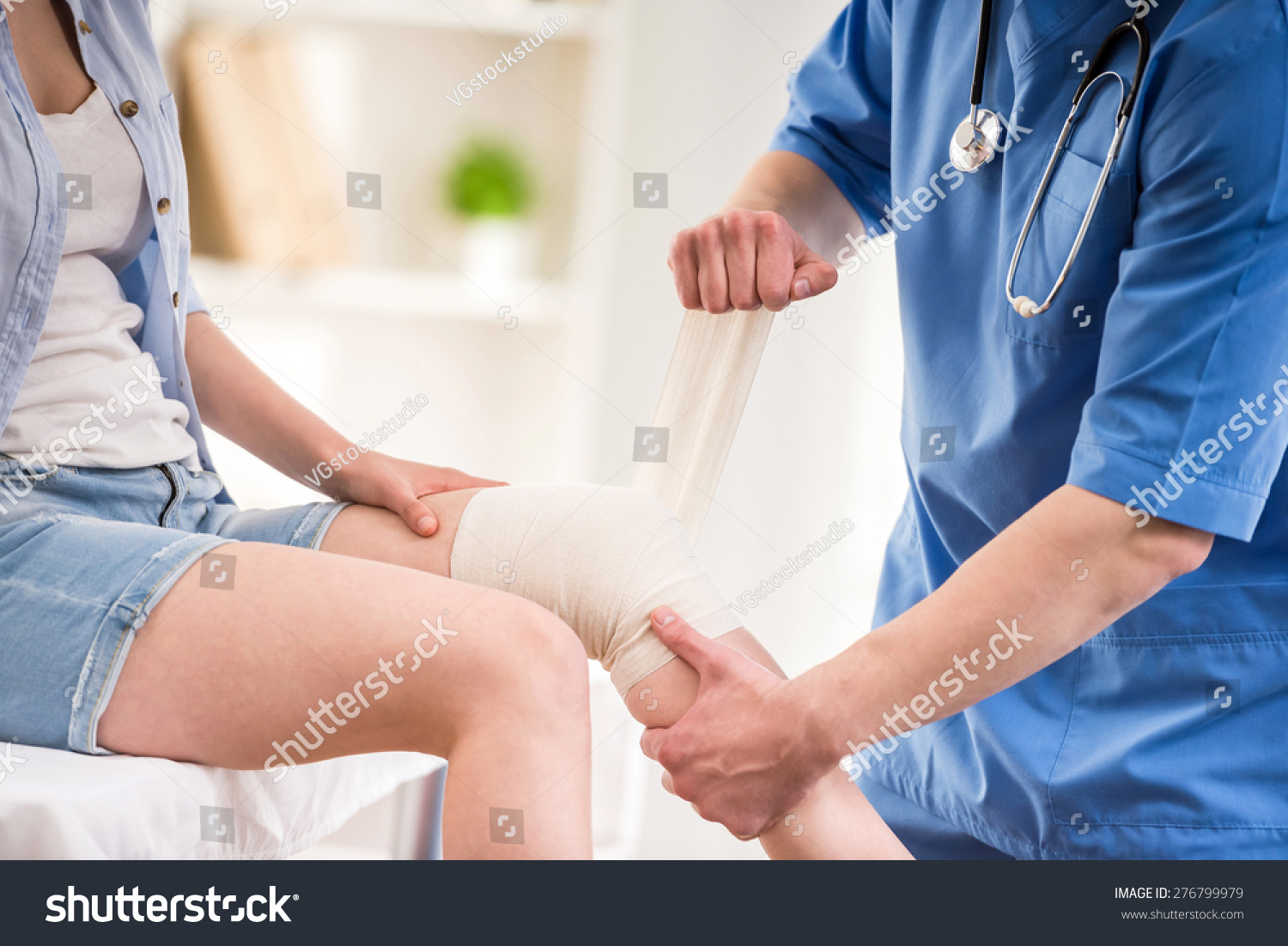 Close-up of male doctor with stethoscope bandaging leg of female ...