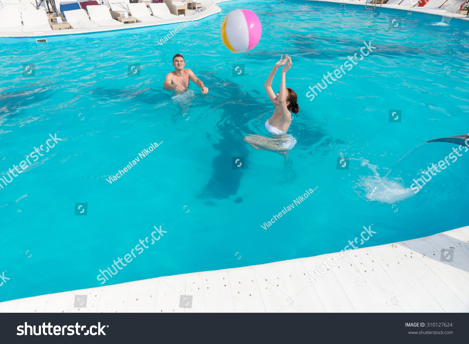 Young couple frolicking in a turquoise blue swimming pool throwing a ...