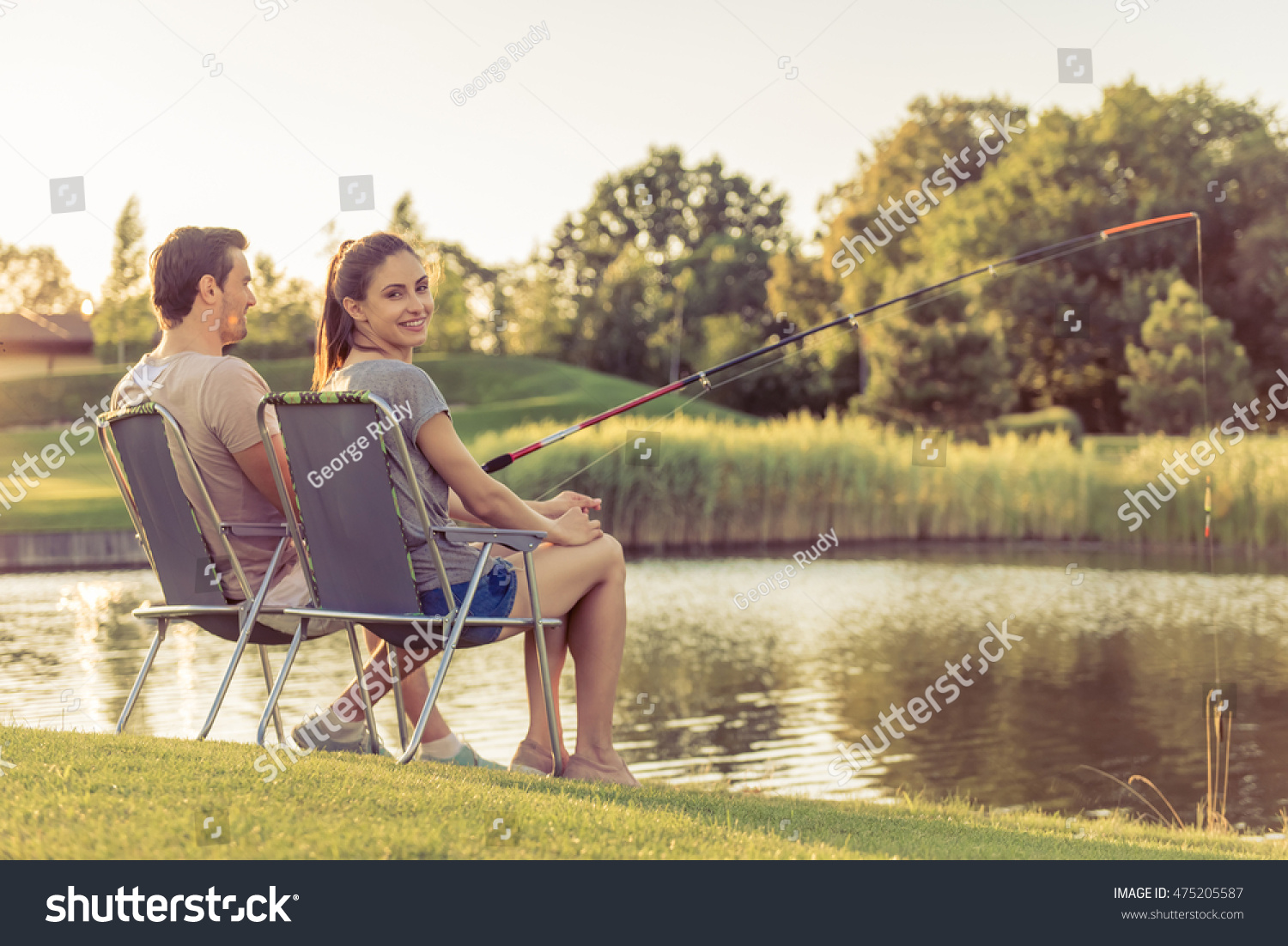 Back view of beautiful couple catching fish in the pond using a fishing ...